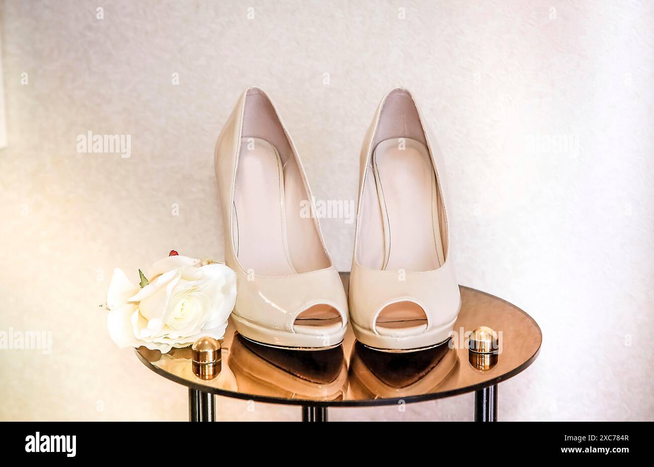 Beige high-heeled peep-toe shoes on a gold table with a white rose ...