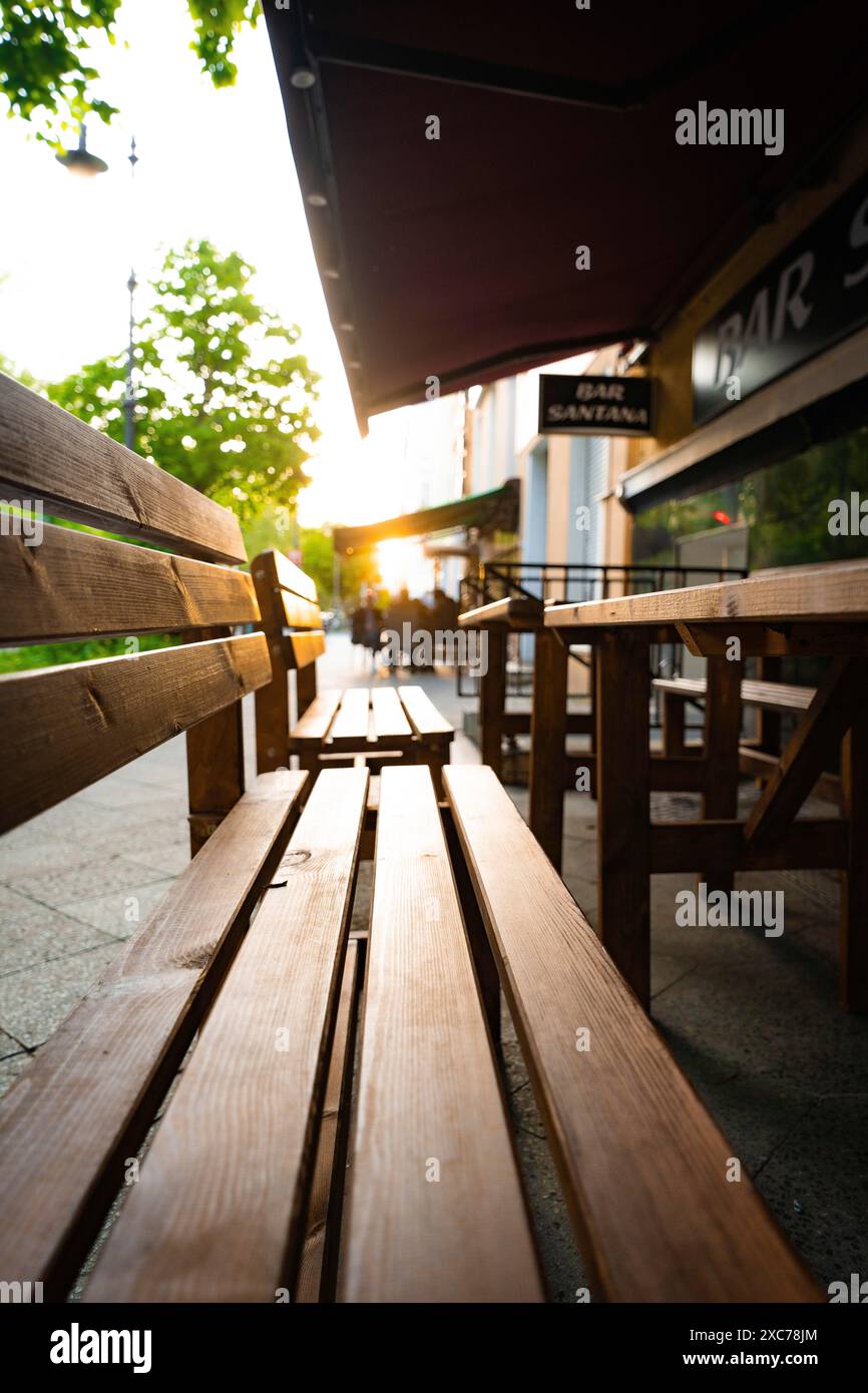 A sun-drenched evening in a street with wooden benches and an outdoor ...