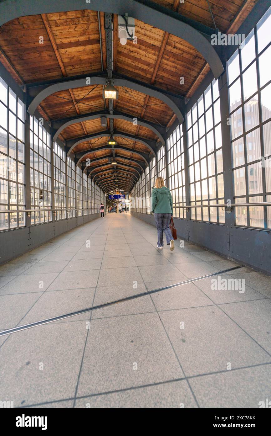 A covered pedestrian bridge in a railway station with glass windows and ...