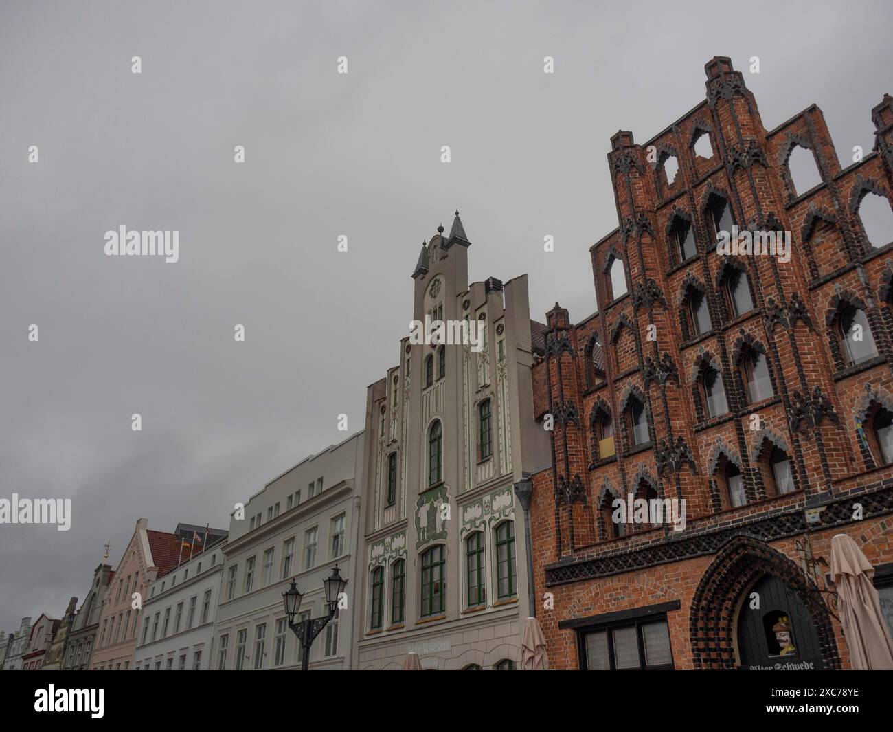 Bay windows and gothic windows in the facades of historic buildings under a cloudy sky, Wismar ...