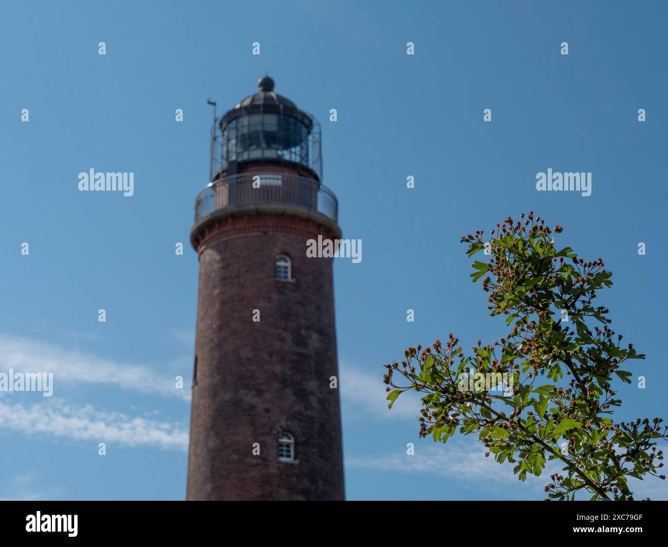 Brick lighthouse with dome and metal railing in front of blue sky and ...