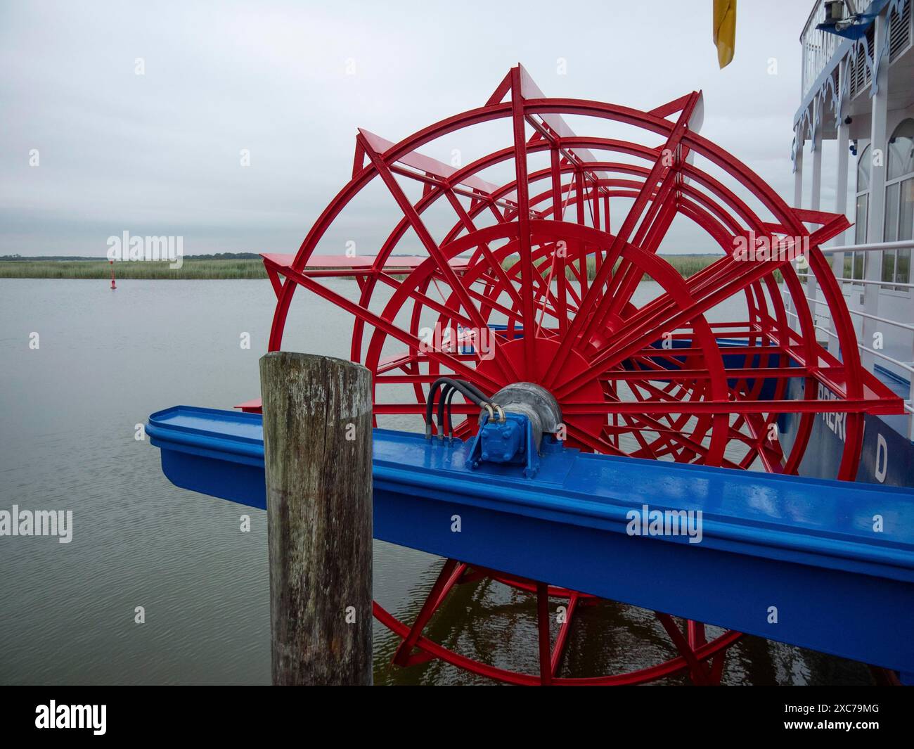 Large red paddle wheel of a boat with blue hull on a river in front of ...