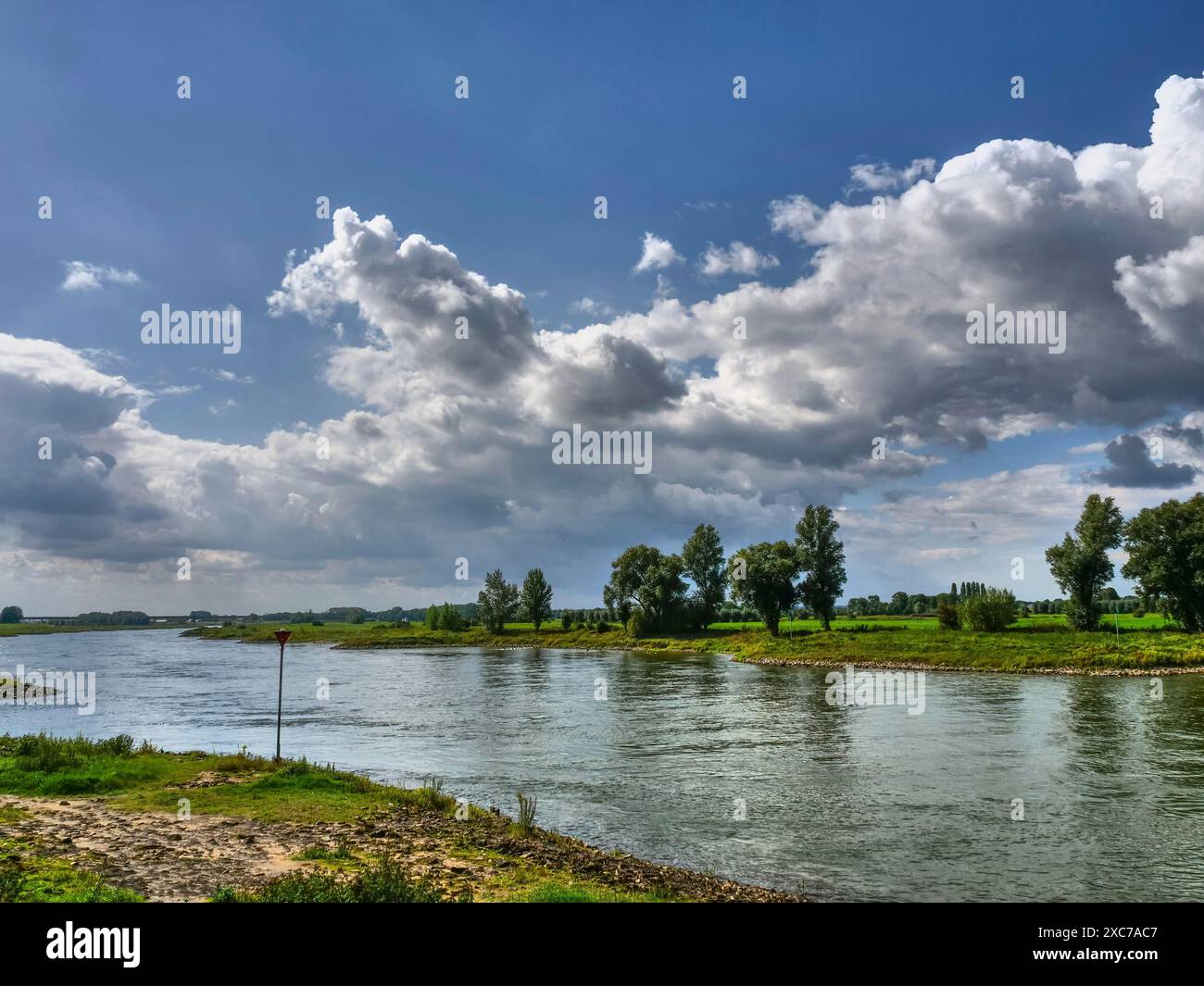 A wide river flows under dramatic clouds, revealing neighbouring green ...