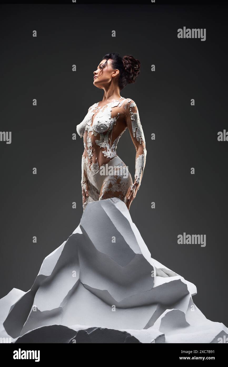 A woman with a sculpted body covered in white paint stands on a large ...