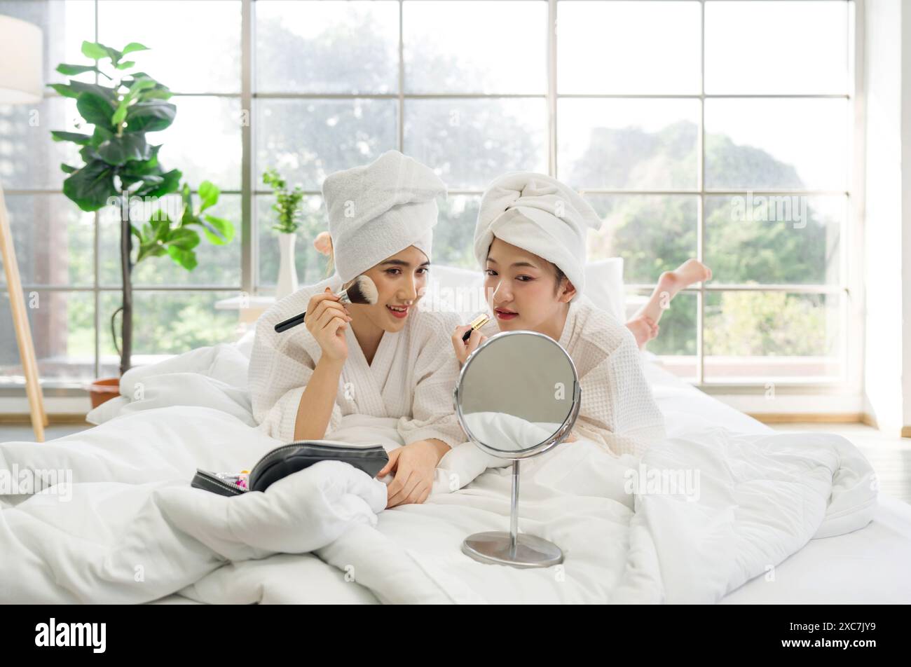 Two asian women are lying relax on a bed in white robe and towel ...