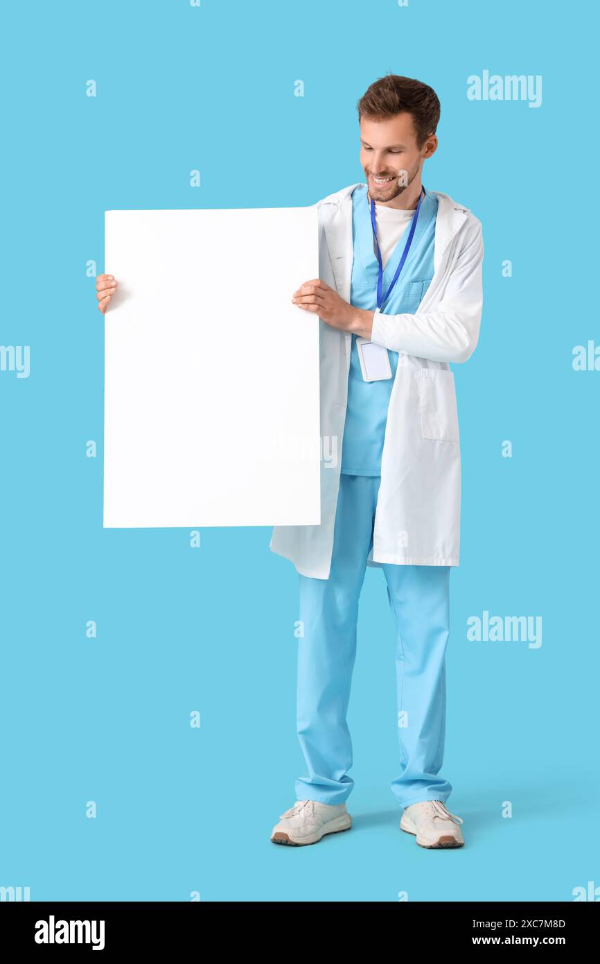 Male medical intern with blank poster on blue background Stock Photo ...
