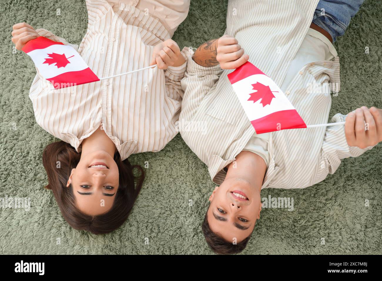 Young couple with flags of Canada lying on floor at home, top view ...