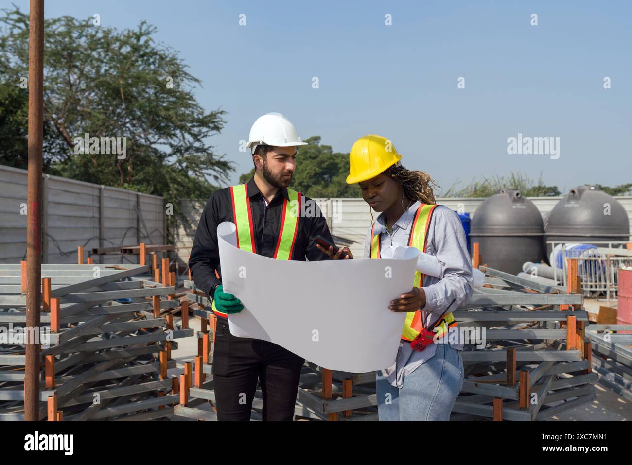 Two construction worker discussing work while holding construction plan ...