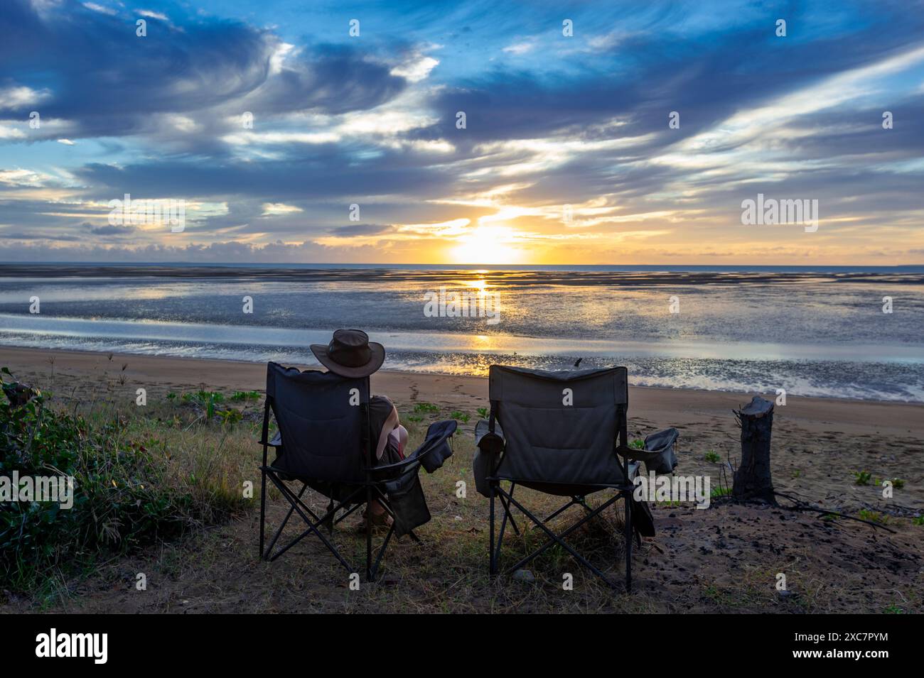 Male camper sitting on a chair on the beach watching an atmospheric ...
