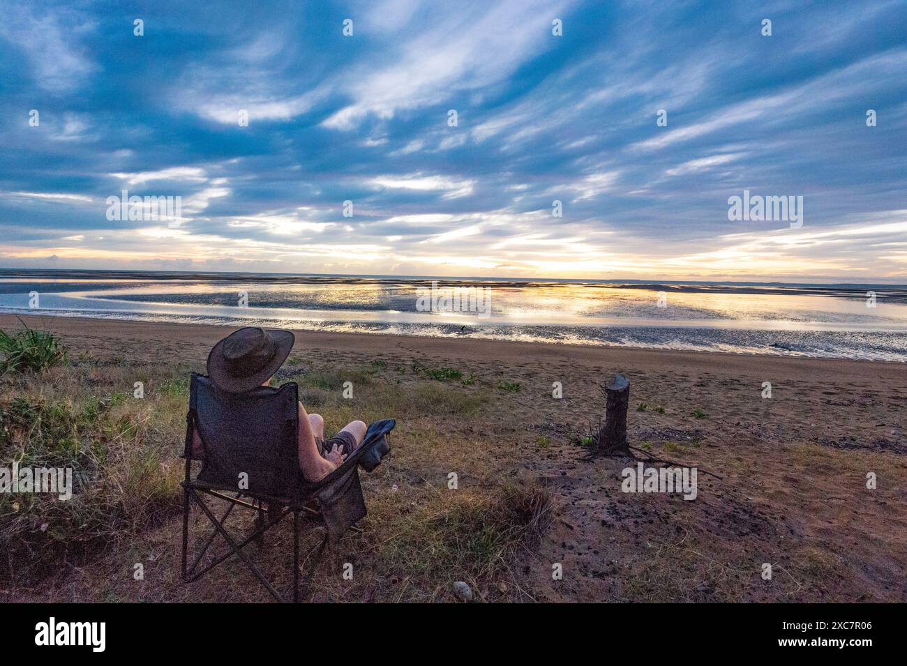 Male camper sitting on a chair on the beach watching an atmospheric ...
