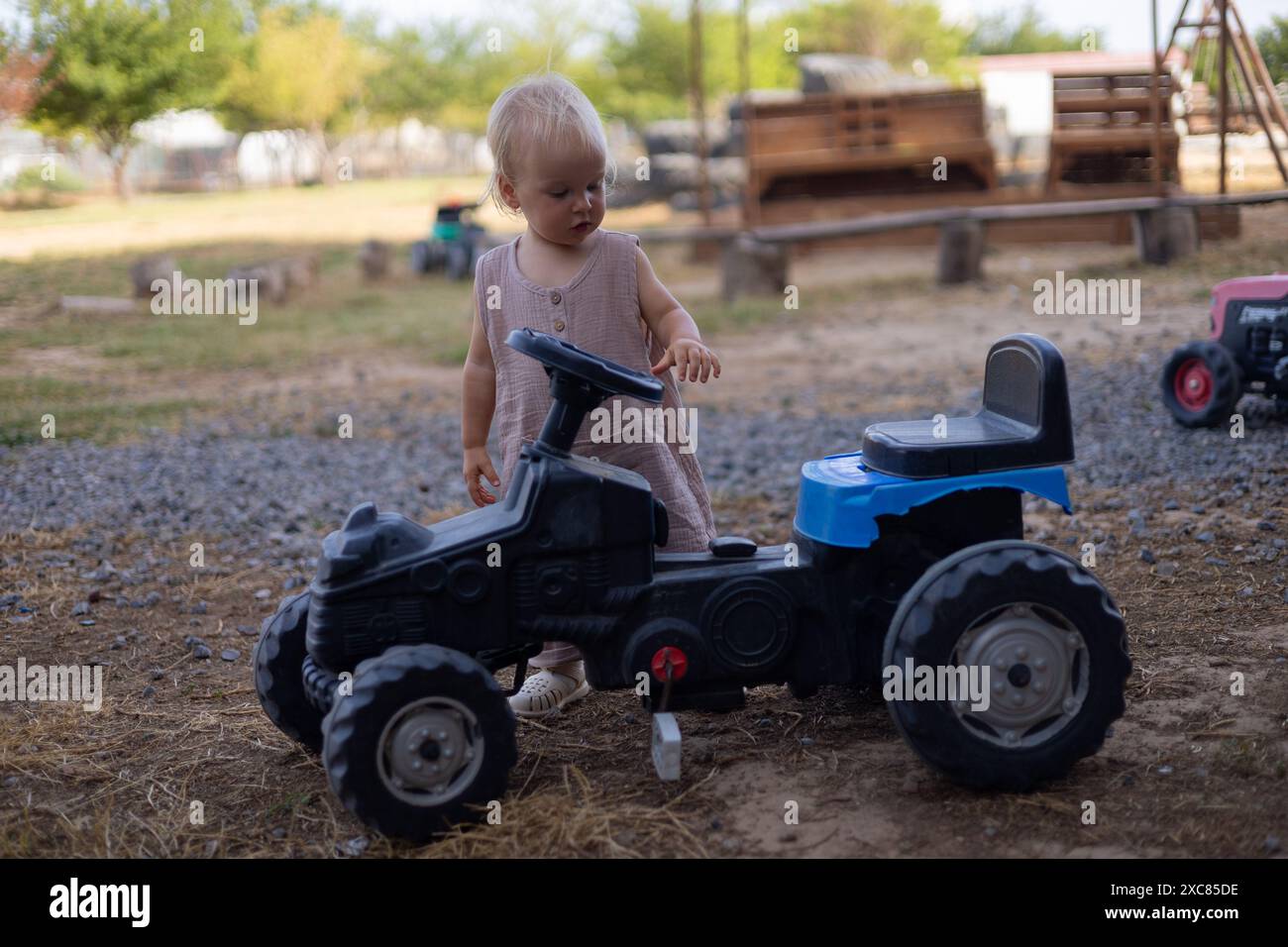 blonde girl playing with miniature tractor on eco farm Stock Photo - Alamy