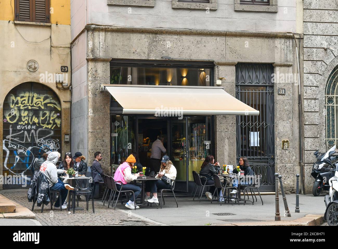 Young people in an outdoor cafè in the central Via Broletto in spring ...