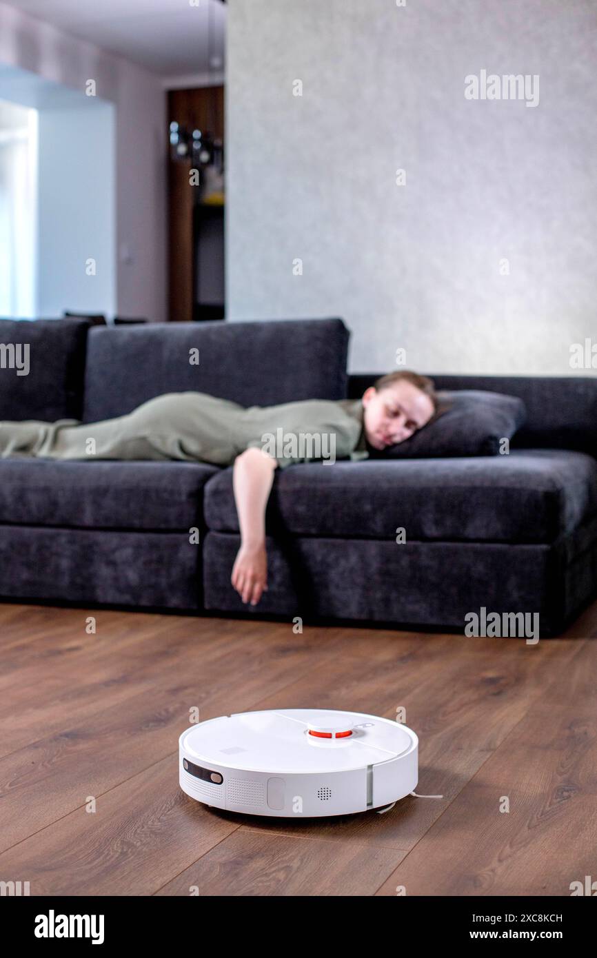Robotic vacuum cleaner cleaning the room while woman resting on sofa ...
