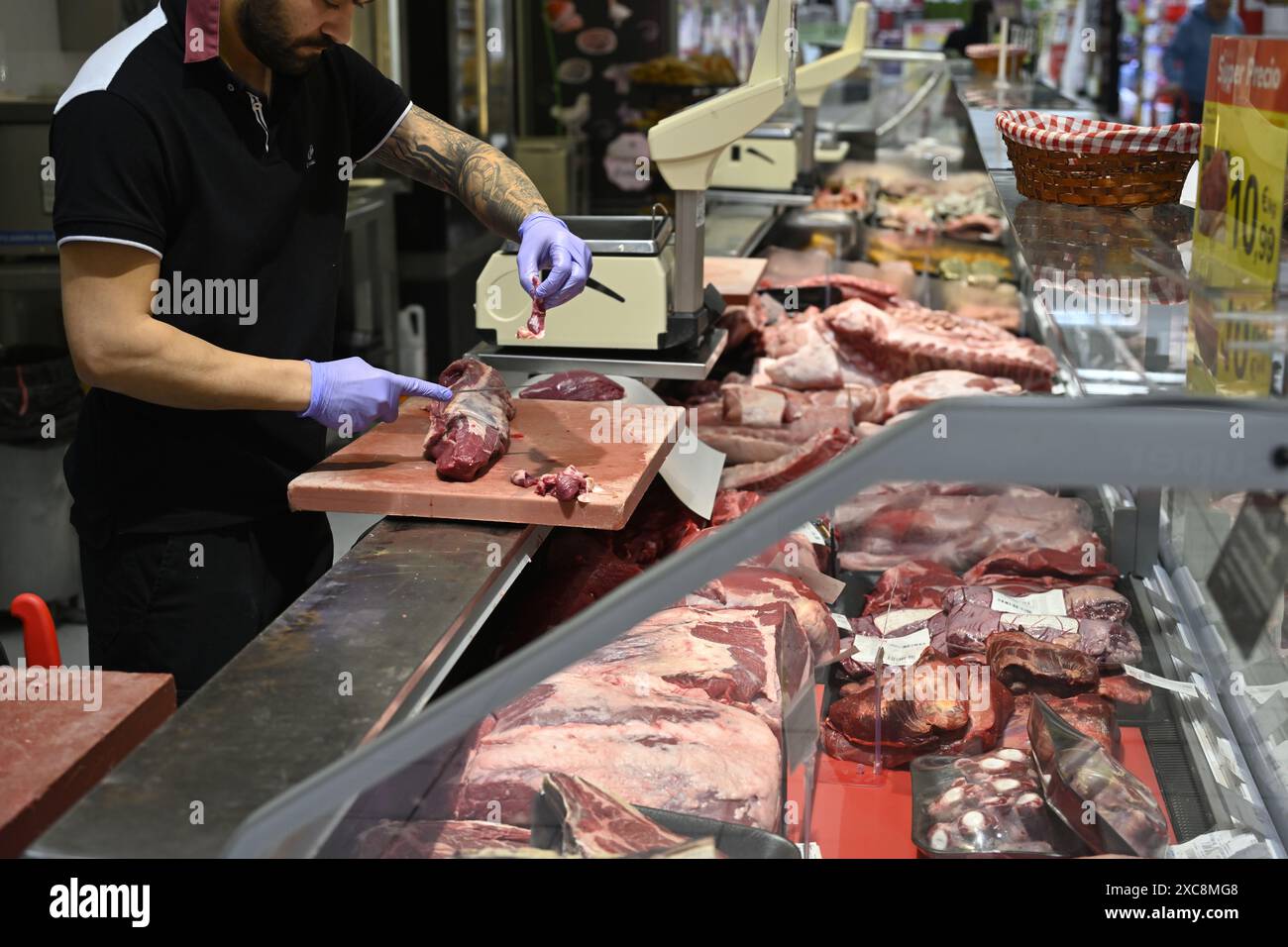 Butcher in supermarket trimming joint of beef for a customer at meat ...