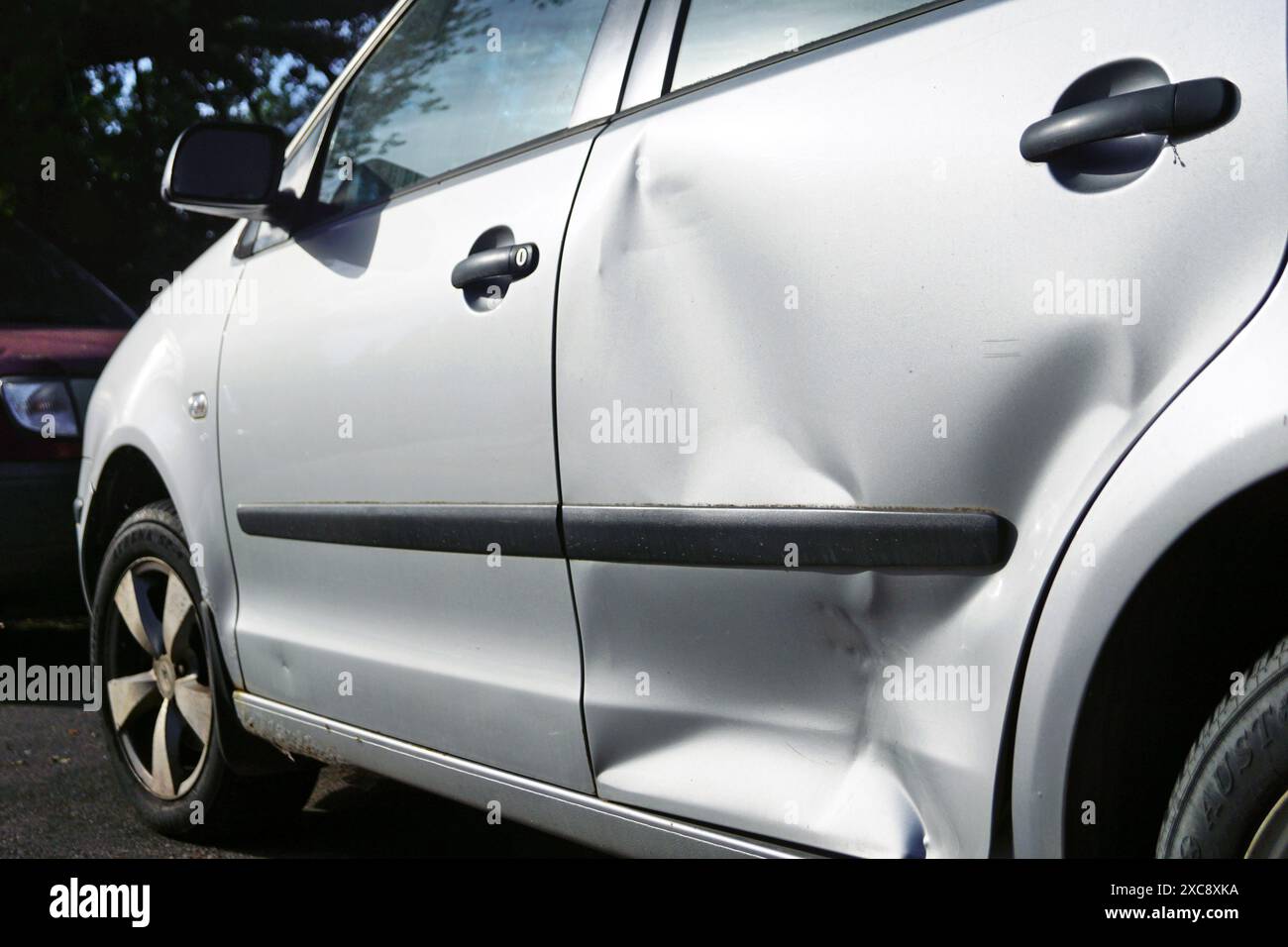 Photo of a silver passenger car with a severe dent on the back door. A ...