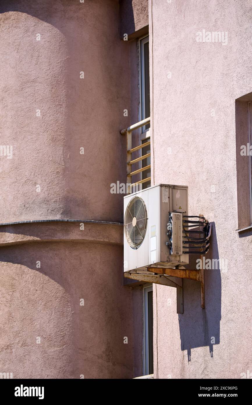 Old air conditioning heat pump outdoor unit against rose wall, vertical ...