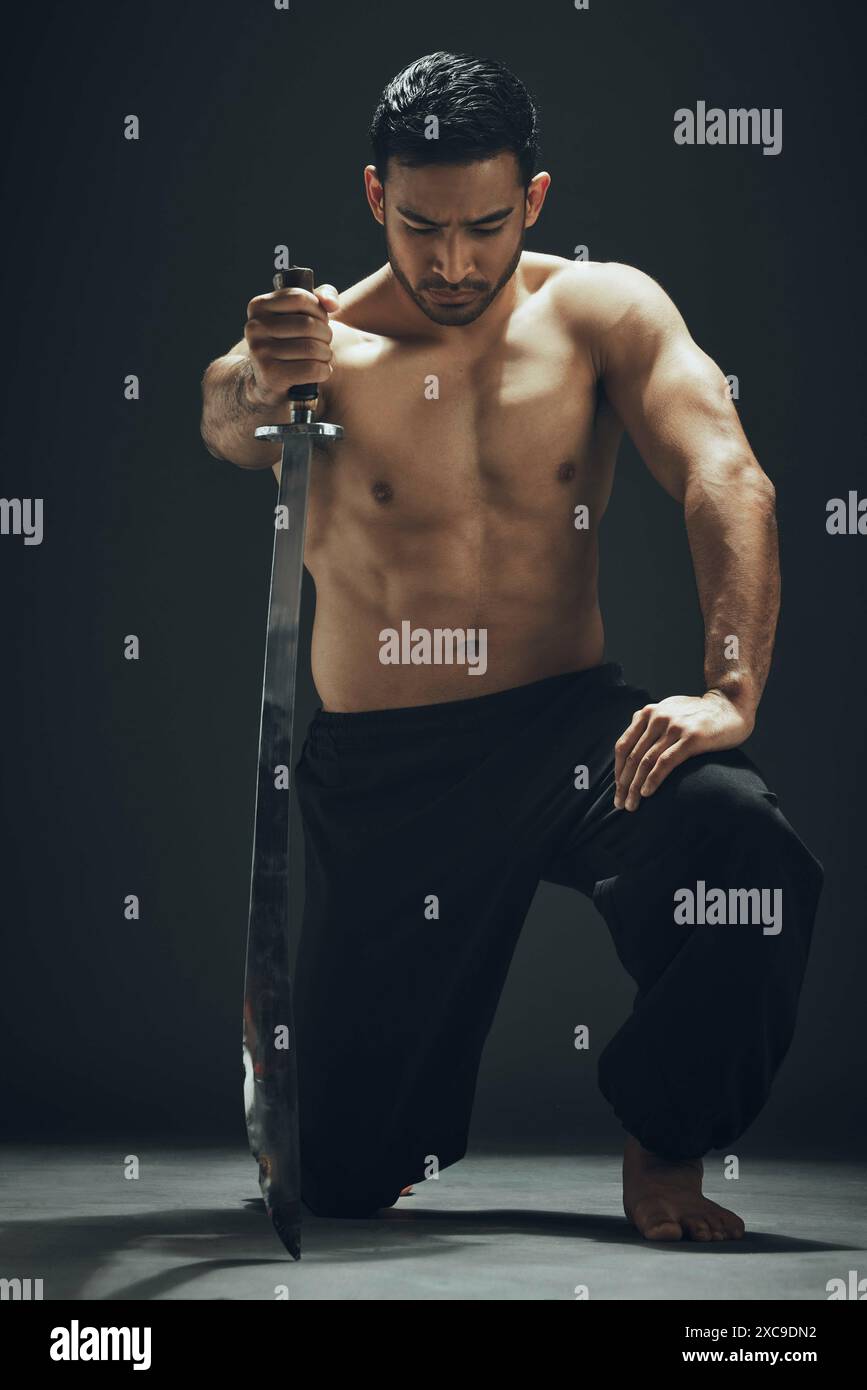 Asian man, kneeling and ninja sword in studio for wellness, calm and ...