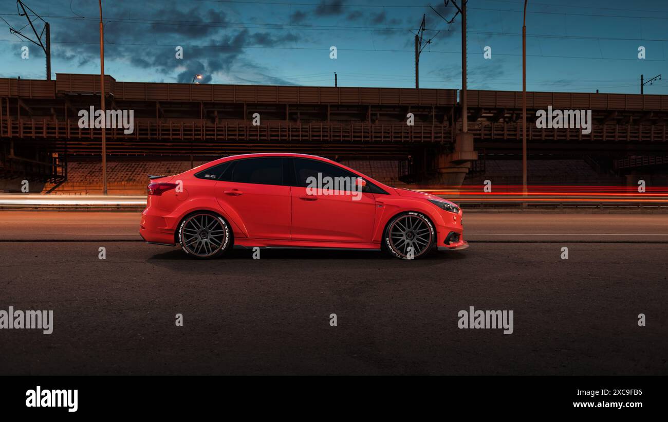 Red mk3 Ford Focus parked on the side of busy road at night. Side ...