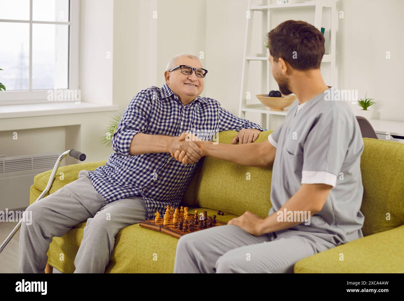 Young nurse man playing chess game with smiling senior elderly at home ...