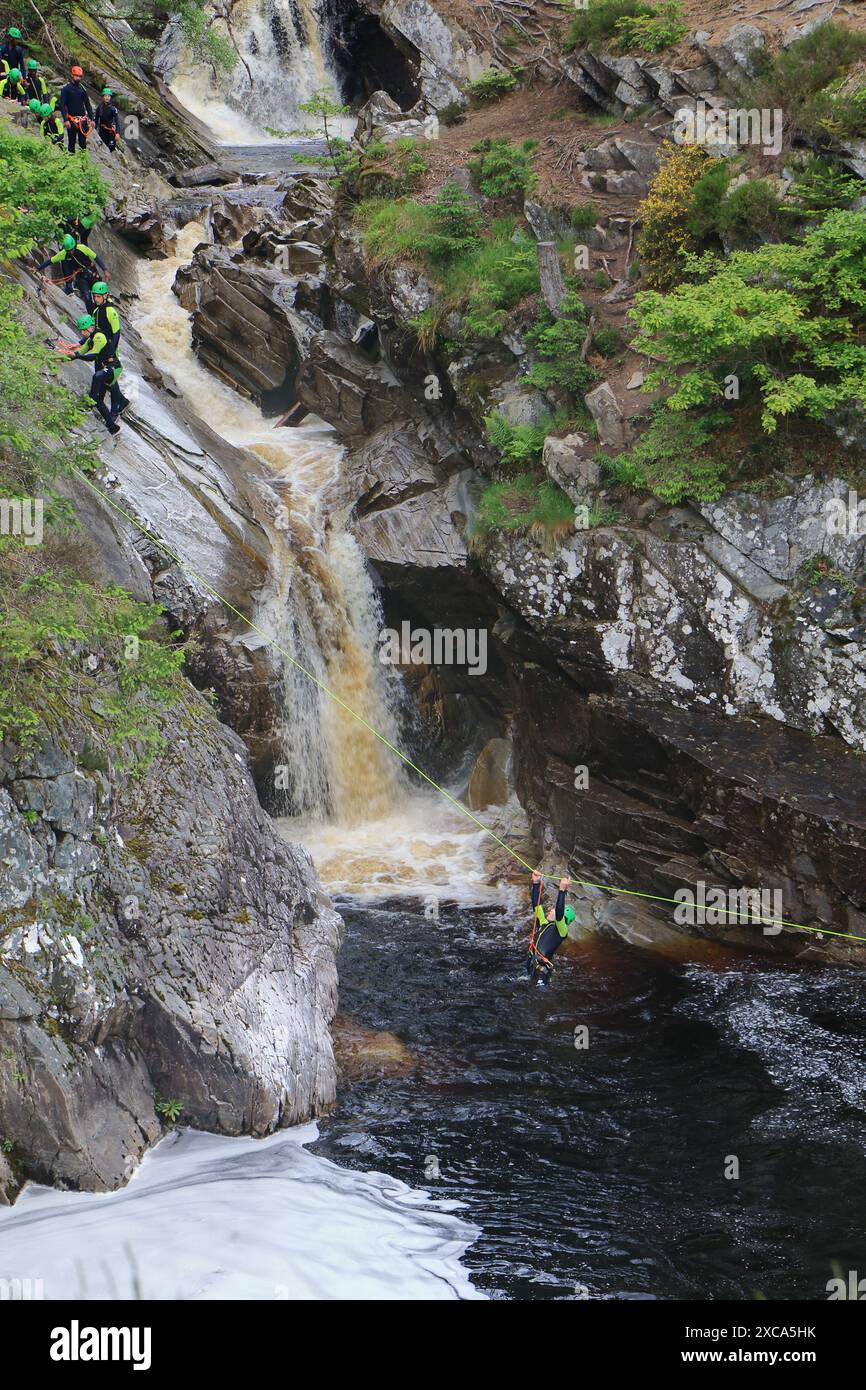People abseiling down rockface and into a pool under the Falls of Bruar ...