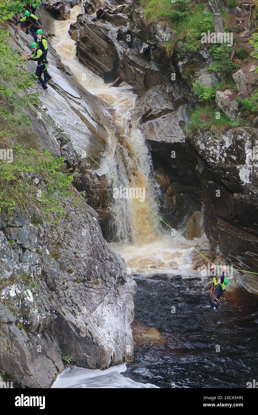 People abseiling down rockface and into a pool under the Falls of Bruar ...