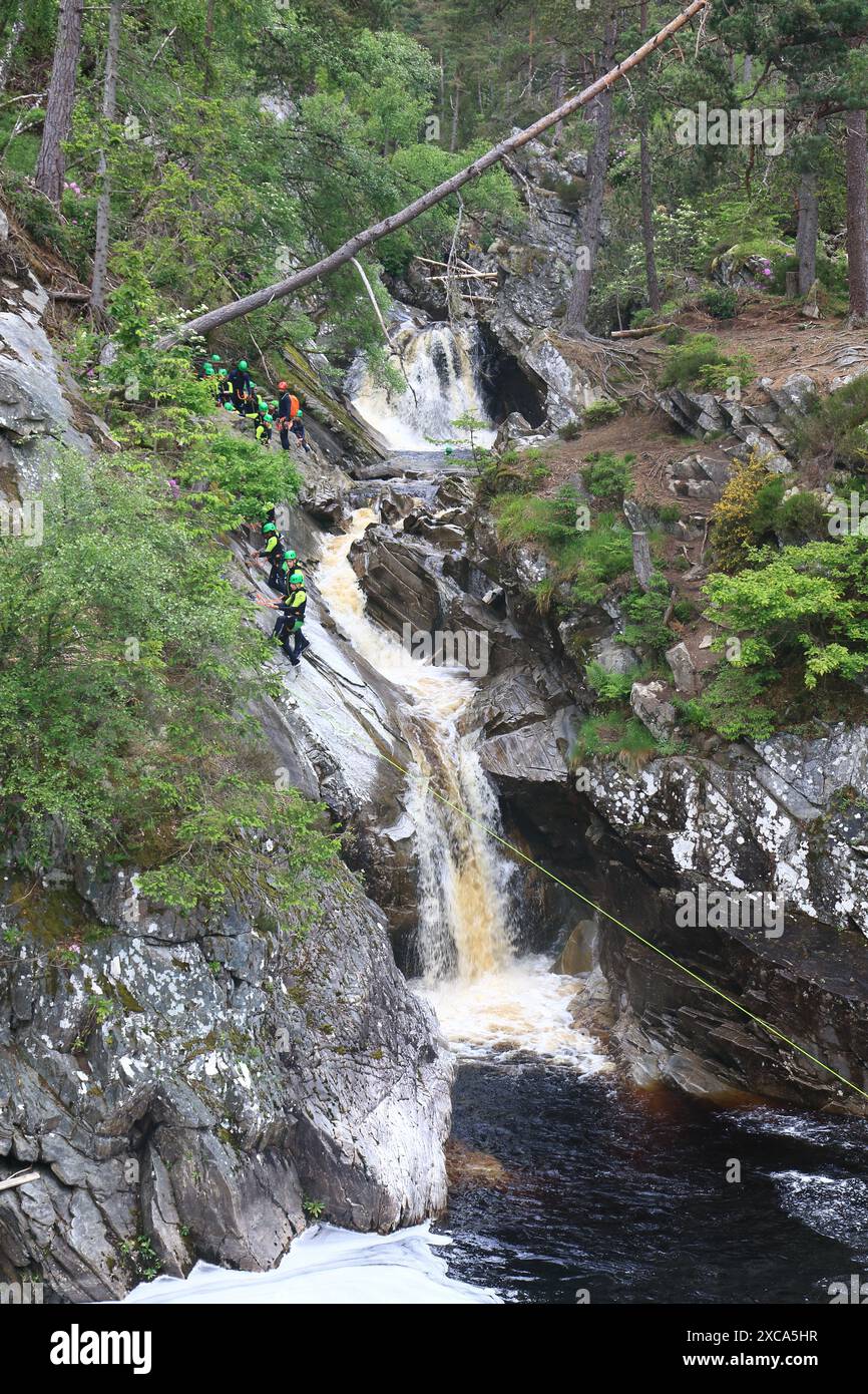 People abseiling down rockface and into a pool under the Falls of Bruar ...