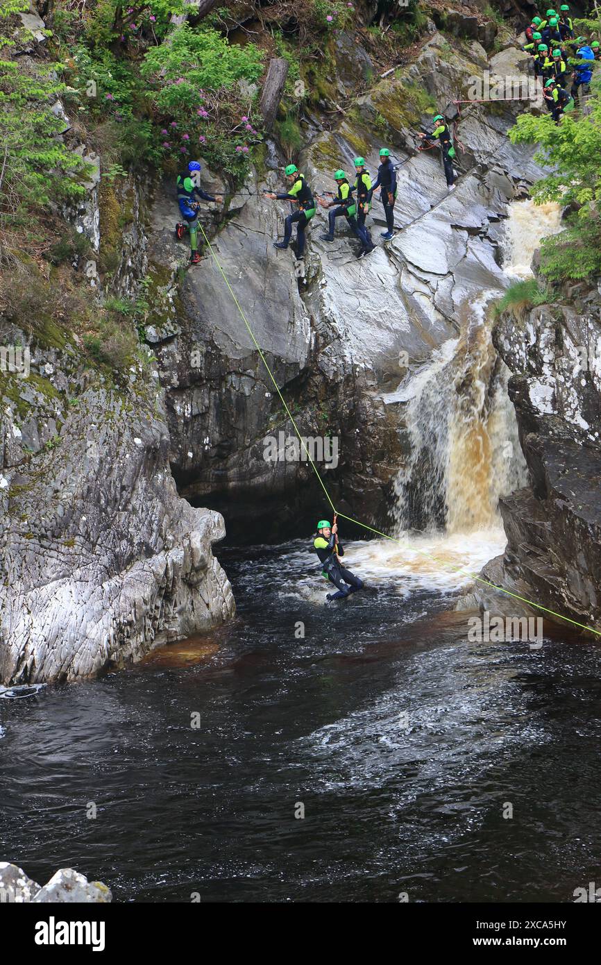 People abseiling down rockface and into a pool under the Falls of Bruar ...
