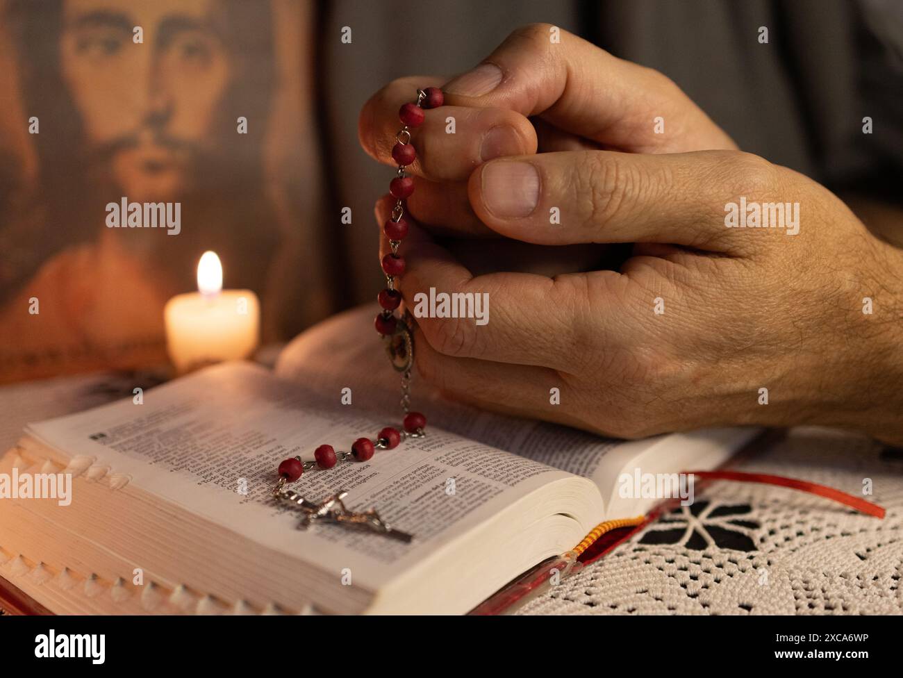 Hands of a young man praying the rosary..Jesus face in the blurred ...