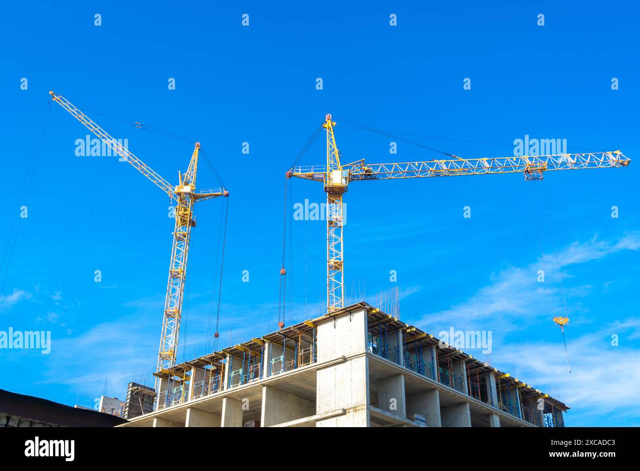 Two cranes are working on a building under a clear blue sky. The cranes ...