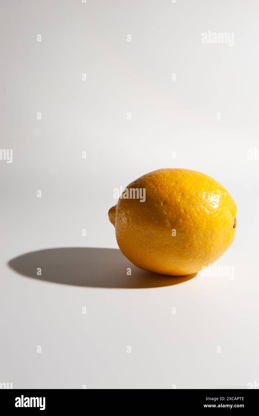 A single, whole, yellow lemon with a hard shadow on a white background ...