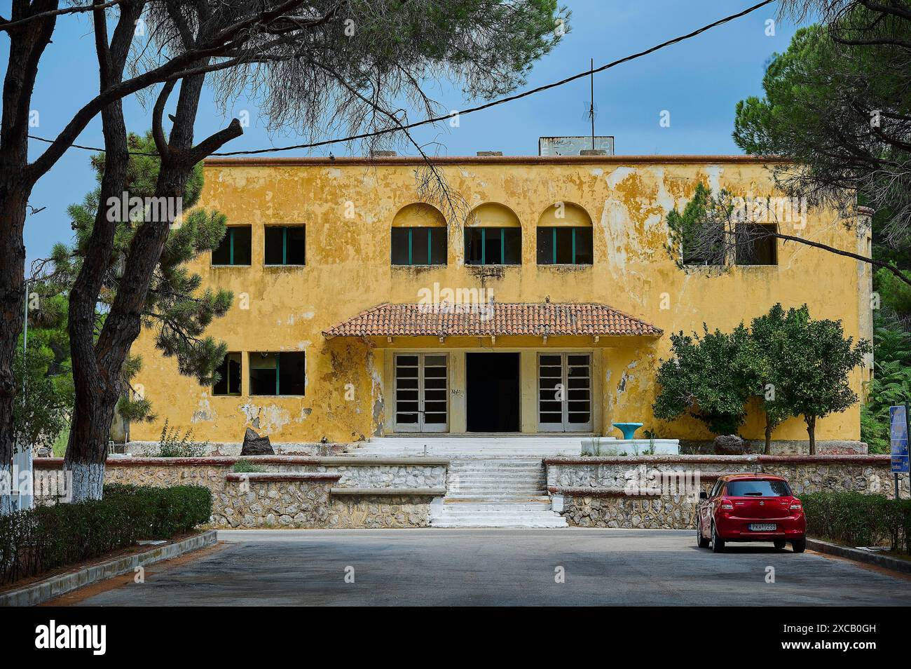 An abandoned yellow house with a damaged facade, surrounded by trees ...
