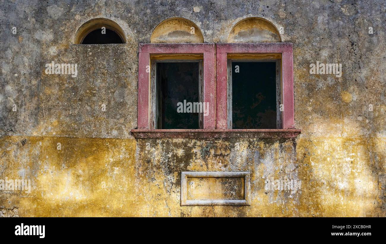 Two old windows in a dilapidated, yellow facade with heavily faded and ...