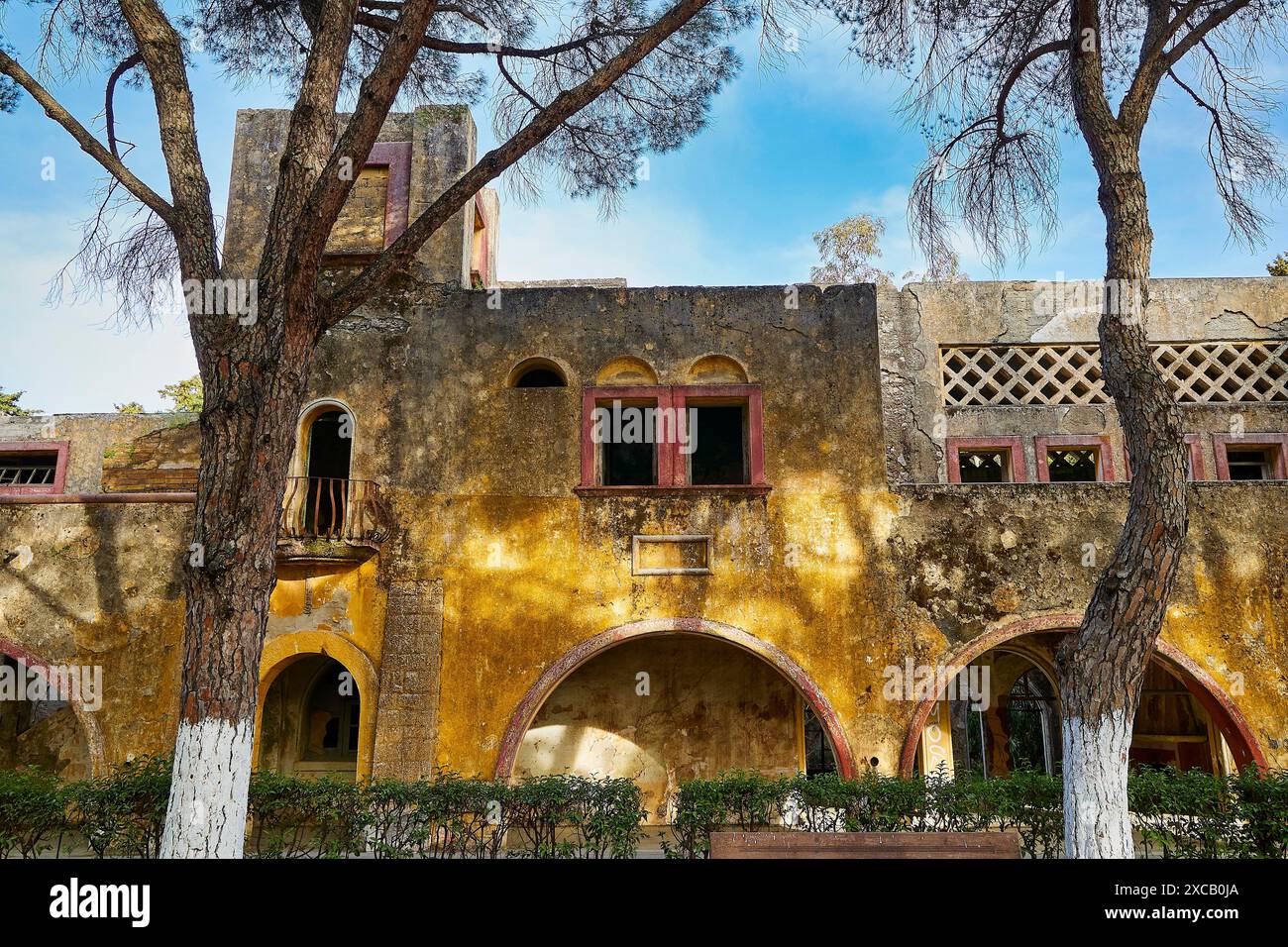 Ruined building with yellow facade and arches flanked by tall trees ...