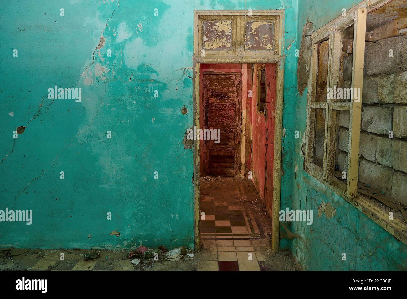 Ruined room with bright blue wall colour and destroyed door, window and ...