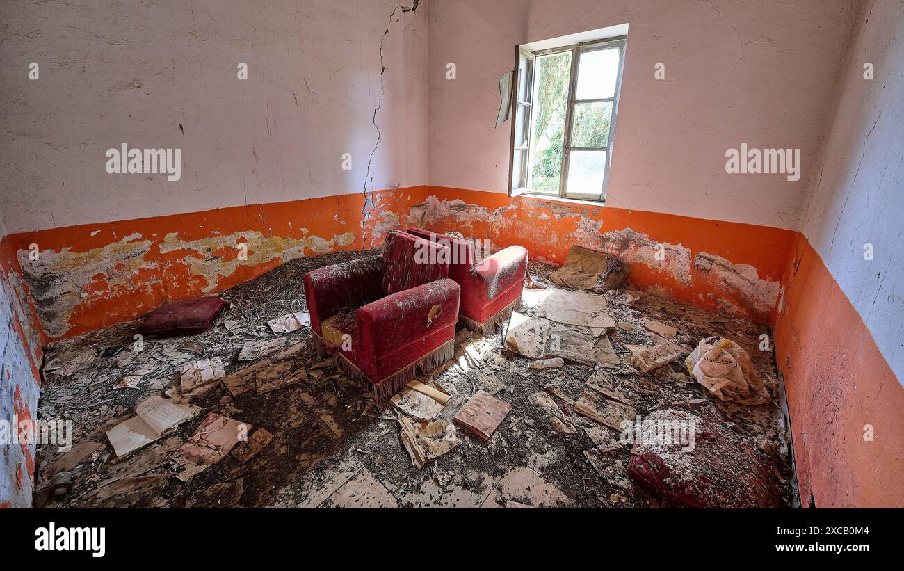 Abandoned room with worn red armchairs and orange-coloured walls. The ...