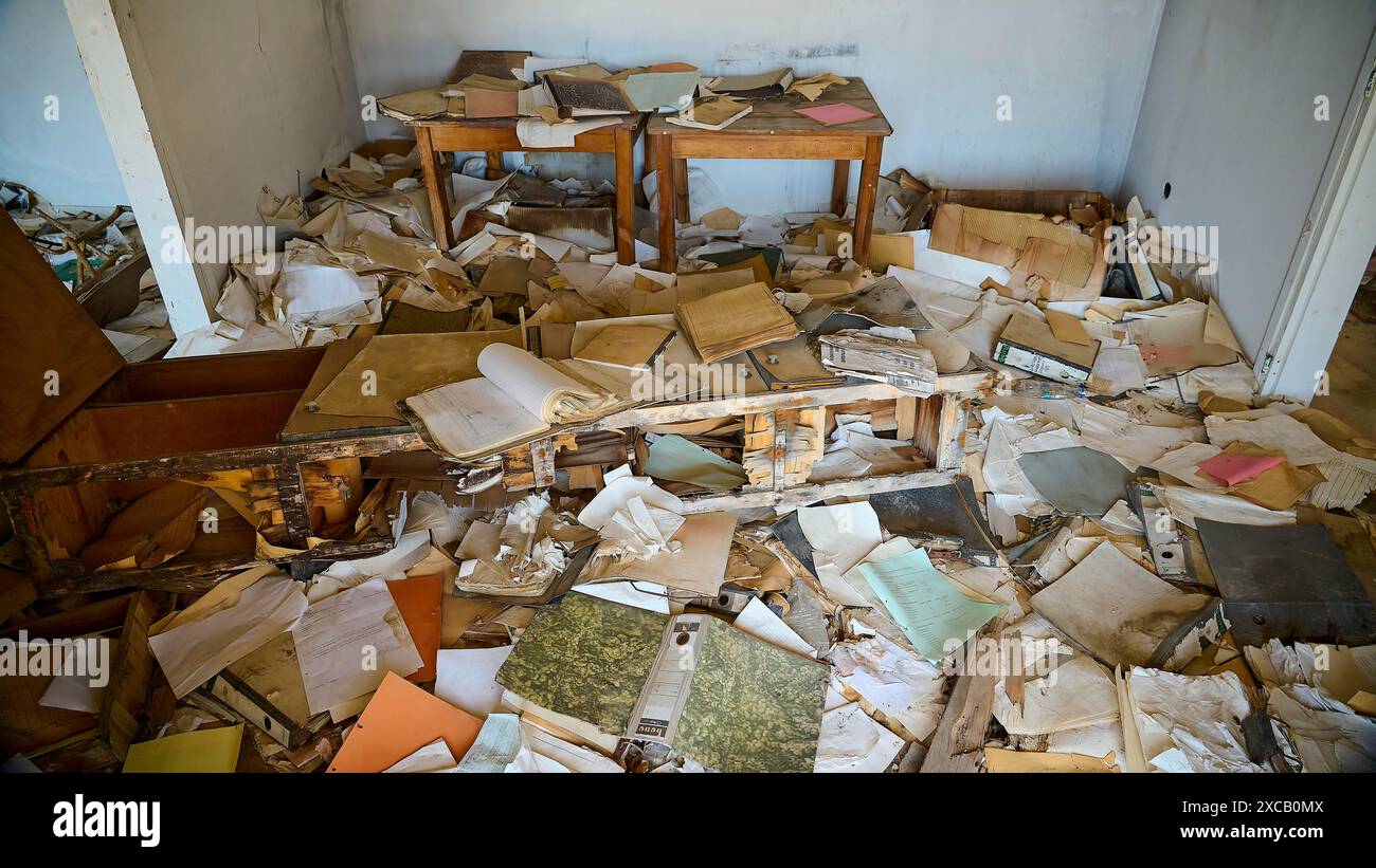 Abandoned room with scattered books and papers, tattered furniture and ...