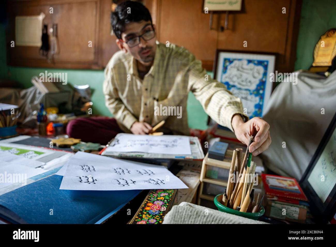 A calligrapher uses a tipped brush to create handwritten designs on ...