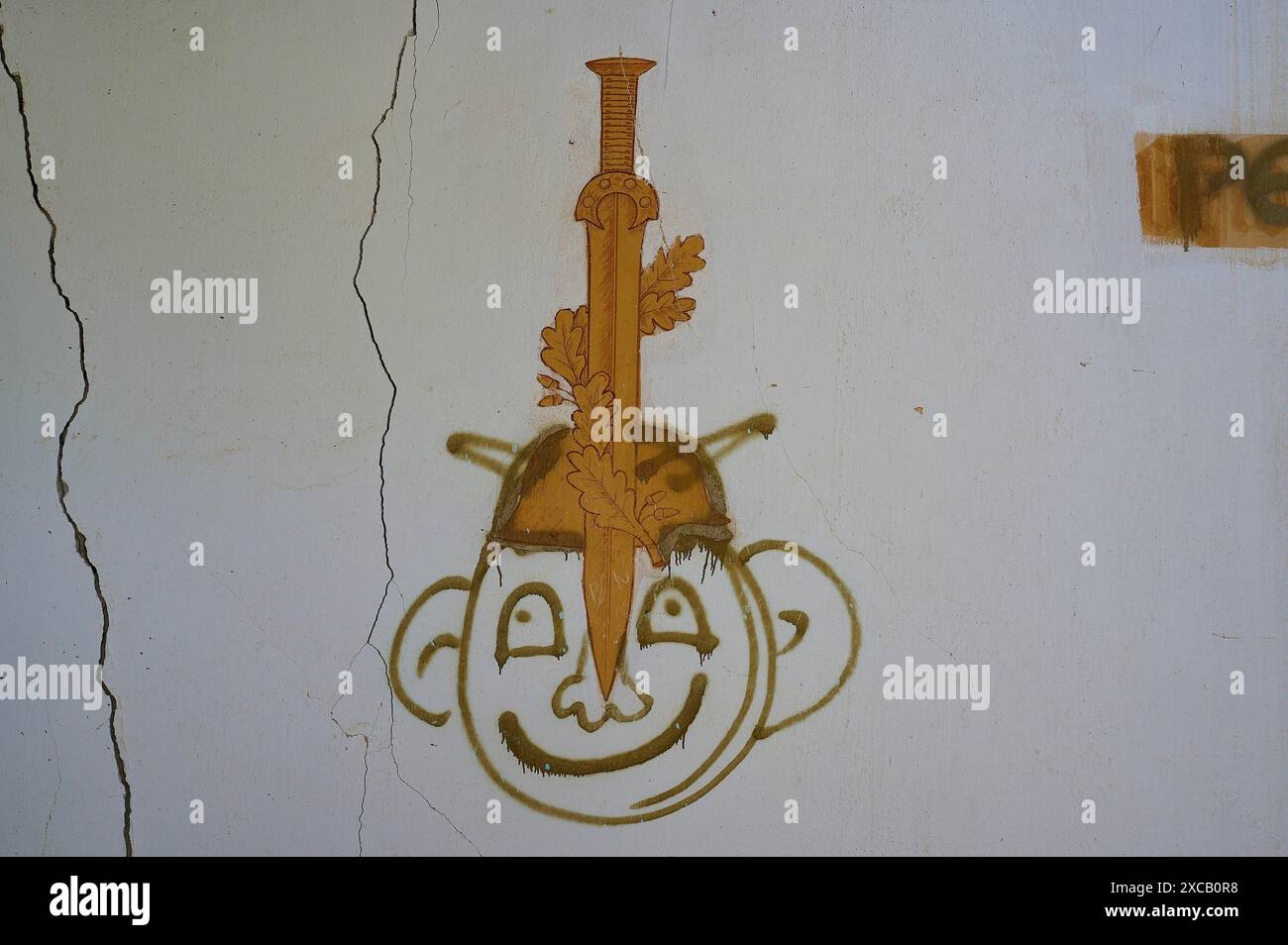 Graffiti of a face with a sword can be seen on a cracked white wall of ...