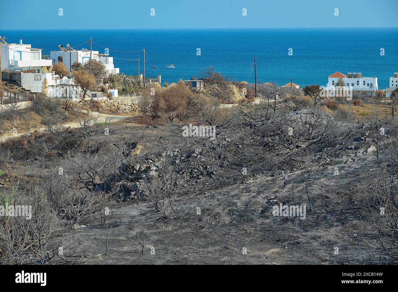 A coastal village with houses surrounded by burnt vegetation, near the ...