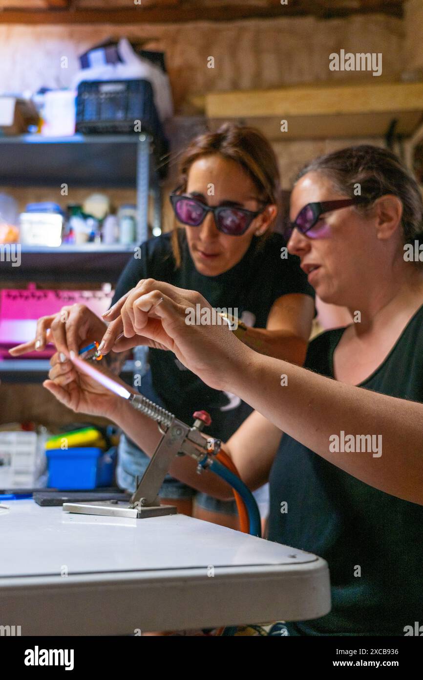 Woman in a glass jewelry creation workshop with the teacher helping her ...