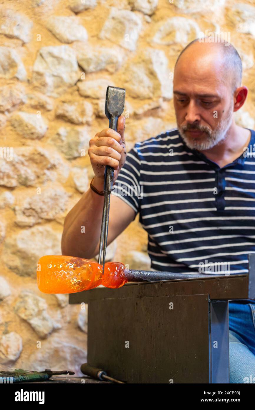 Artisan man shaping a blown glass vase in an artisanal glass blowing ...