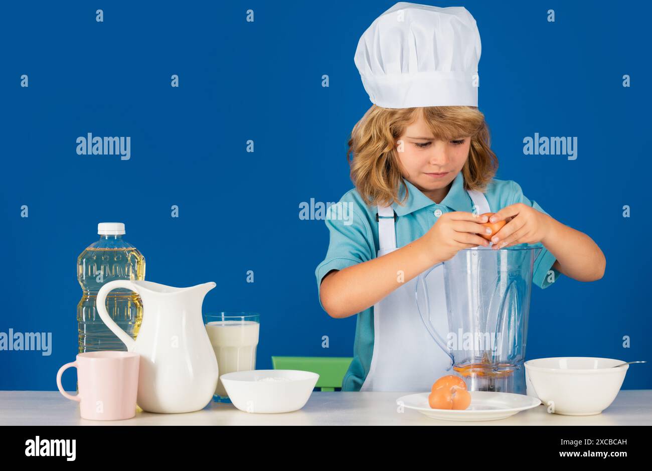 Child chef cook prepares food in isolated blue studio background. Kids ...