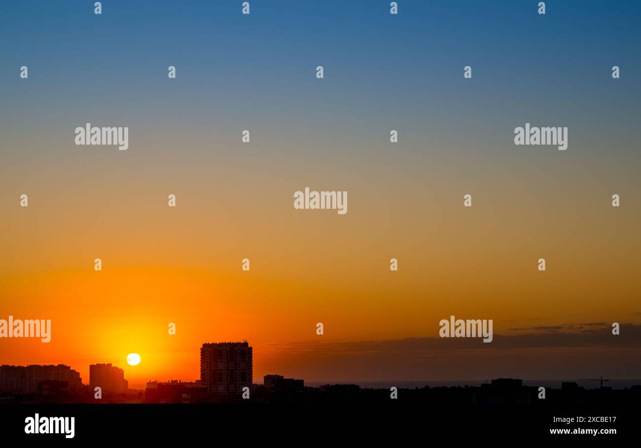 Clear skies over the silhouetted rooftops of a seaside town. The sun ...