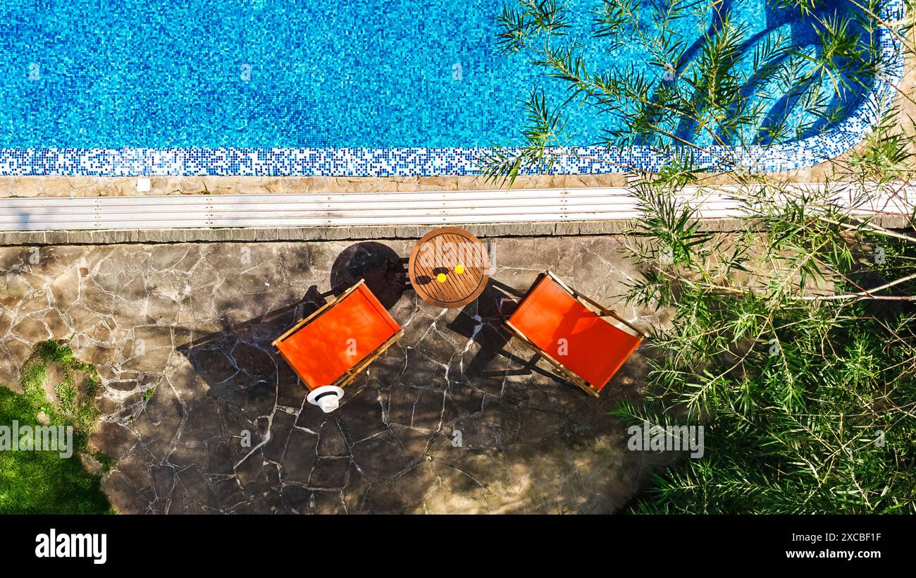 Swimming pool with blue water and sunbed deckchairs aerial top view ...