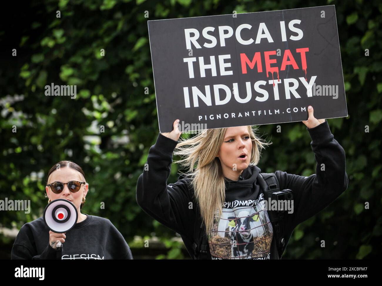 Protesters shout through a megaphone and hold up a placard saying ...