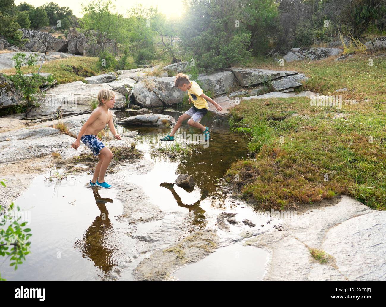 Two Caucasian children playing jumping over a stream in summer in ...