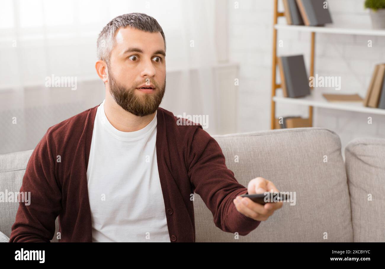 Shocked Man Sitting on Couch Holding Remote Control Stock Photo - Alamy