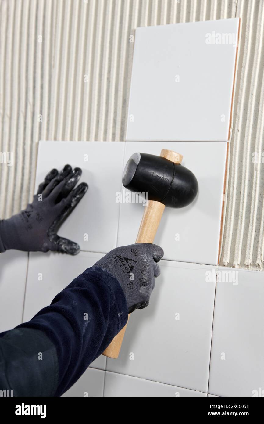 Laying tiles on glue mortar-covered wall using rubber mallet, new homes ...