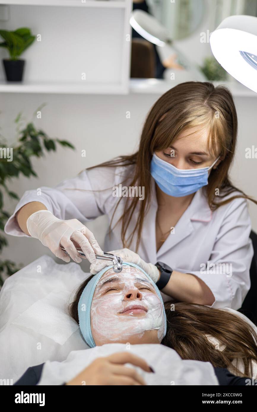 Young dermatologist performing a soothing face massage on a young woman which face is covered ...