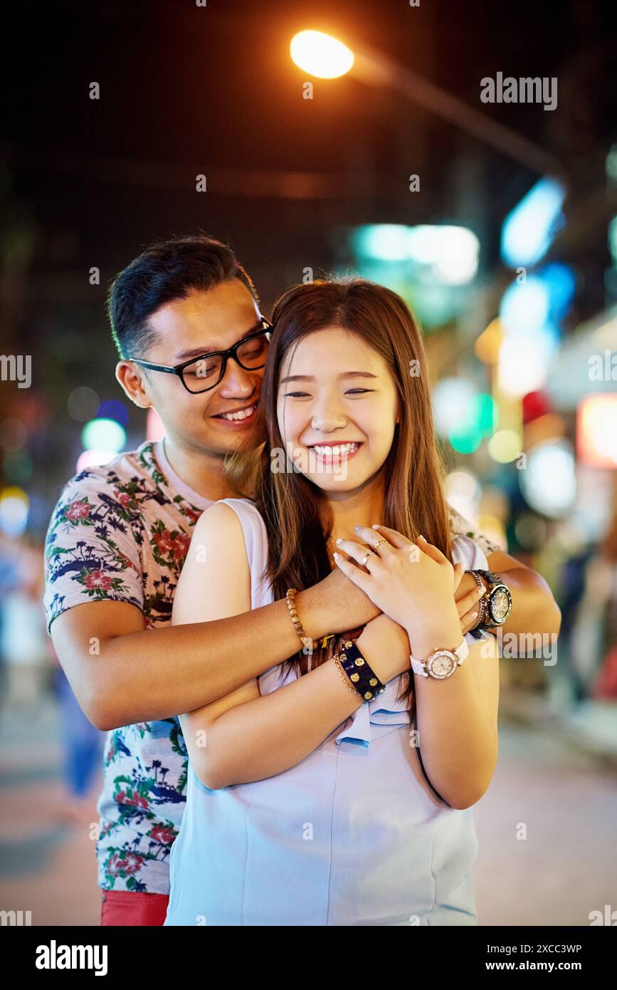 Asian couple, hug and city travel with love or bokeh lights at night or explore Thailand ...